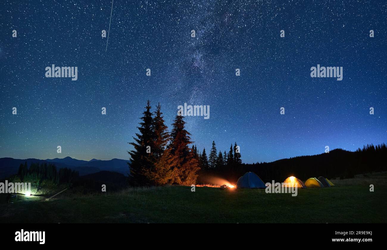 Night camping in mountains under starry sky. Tourist tents in campsite near burning campfire ...