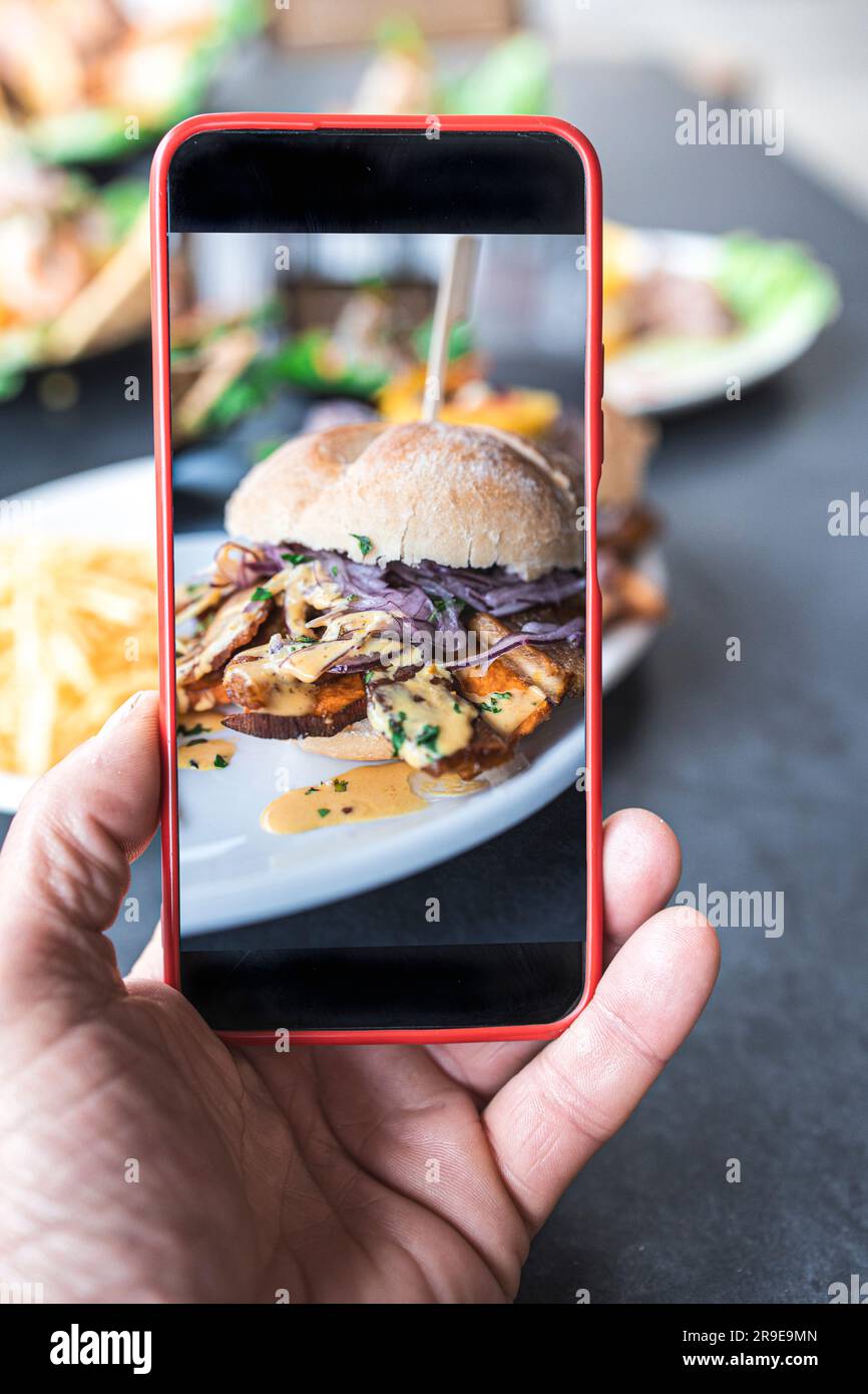 Food blogger using a smart phone taking photos of a delicious burger to ...