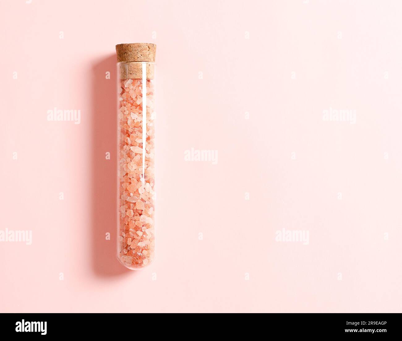 Himalayan pink salt in a glass container with cork on pink background ...