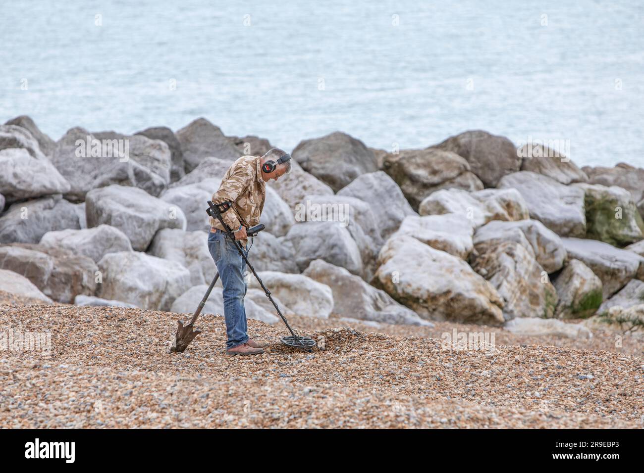 A man using a metal detector on a shingle beach Stock Photo - Alamy