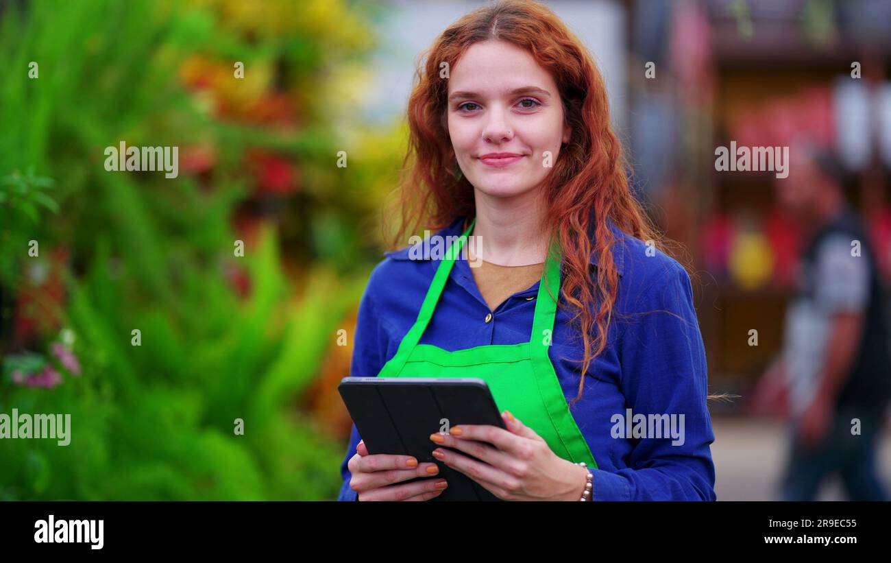 Portrait of a young female employee manager holding tablet and wearing Green Apron inside a ...