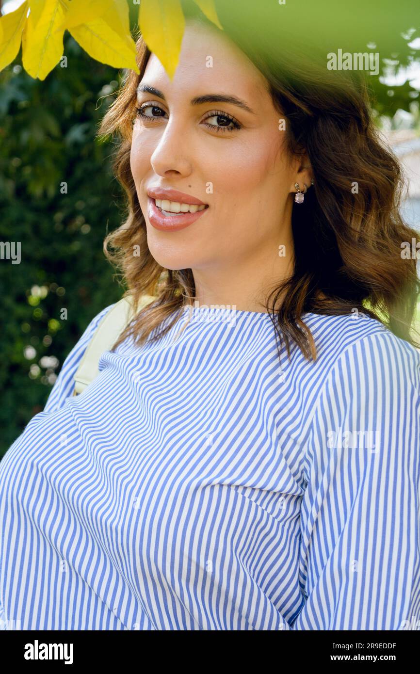 vertical portrait of young latin woman of argentinian ethnicity, standing smiling and looking at ...