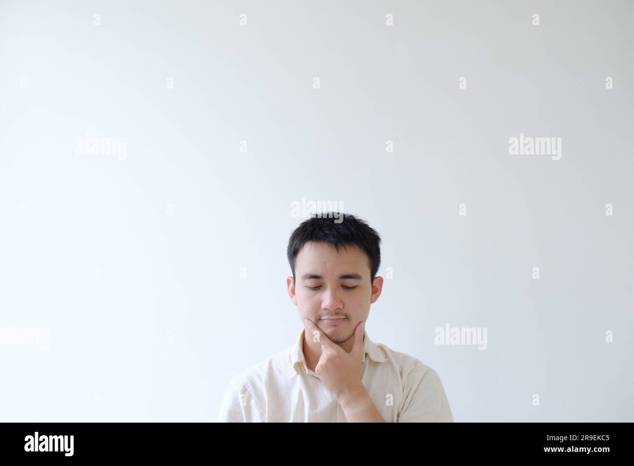 Wide shot of a young Asian man wearing a beige shirt is thinking by ...