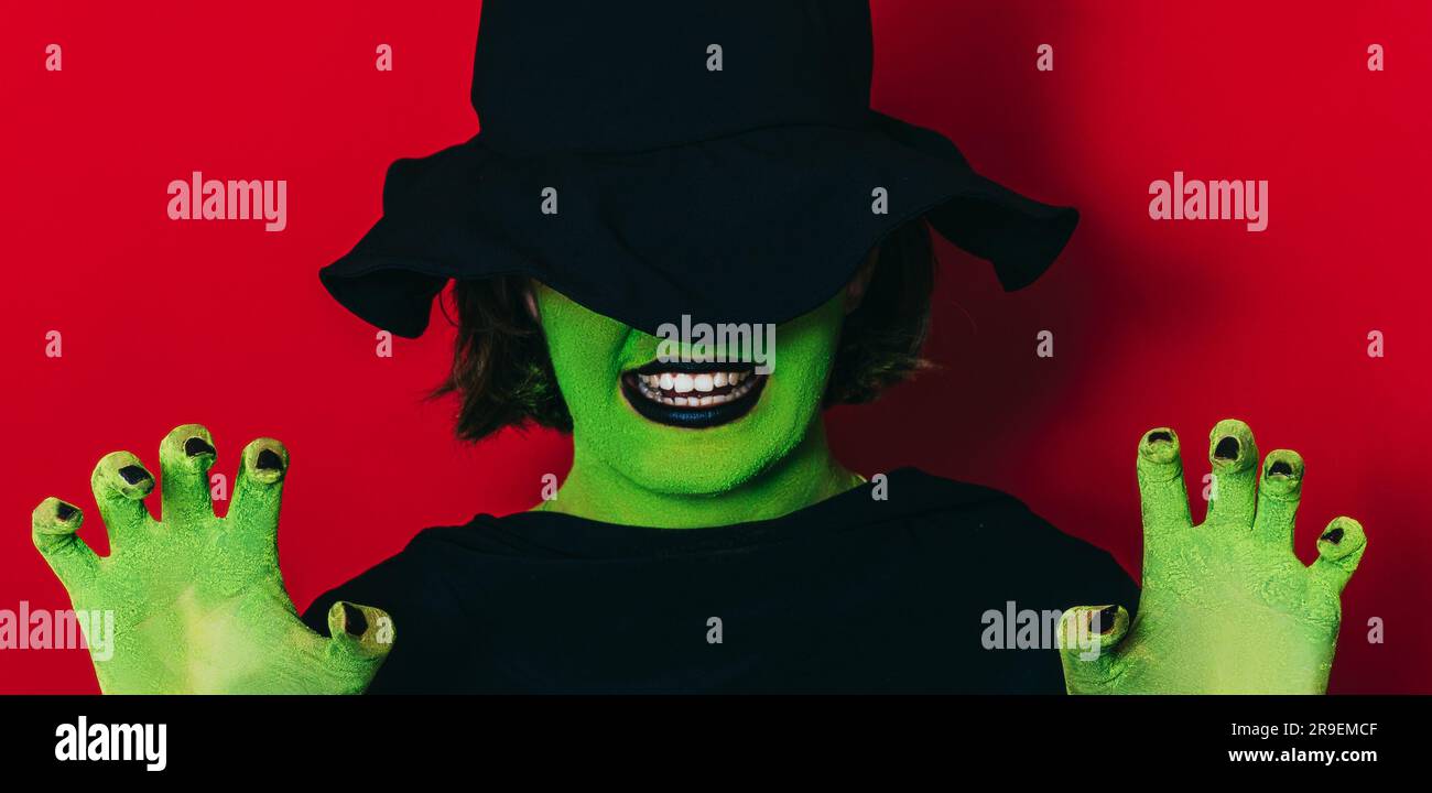 Lady scares in witch costume with green skin color against red ...
