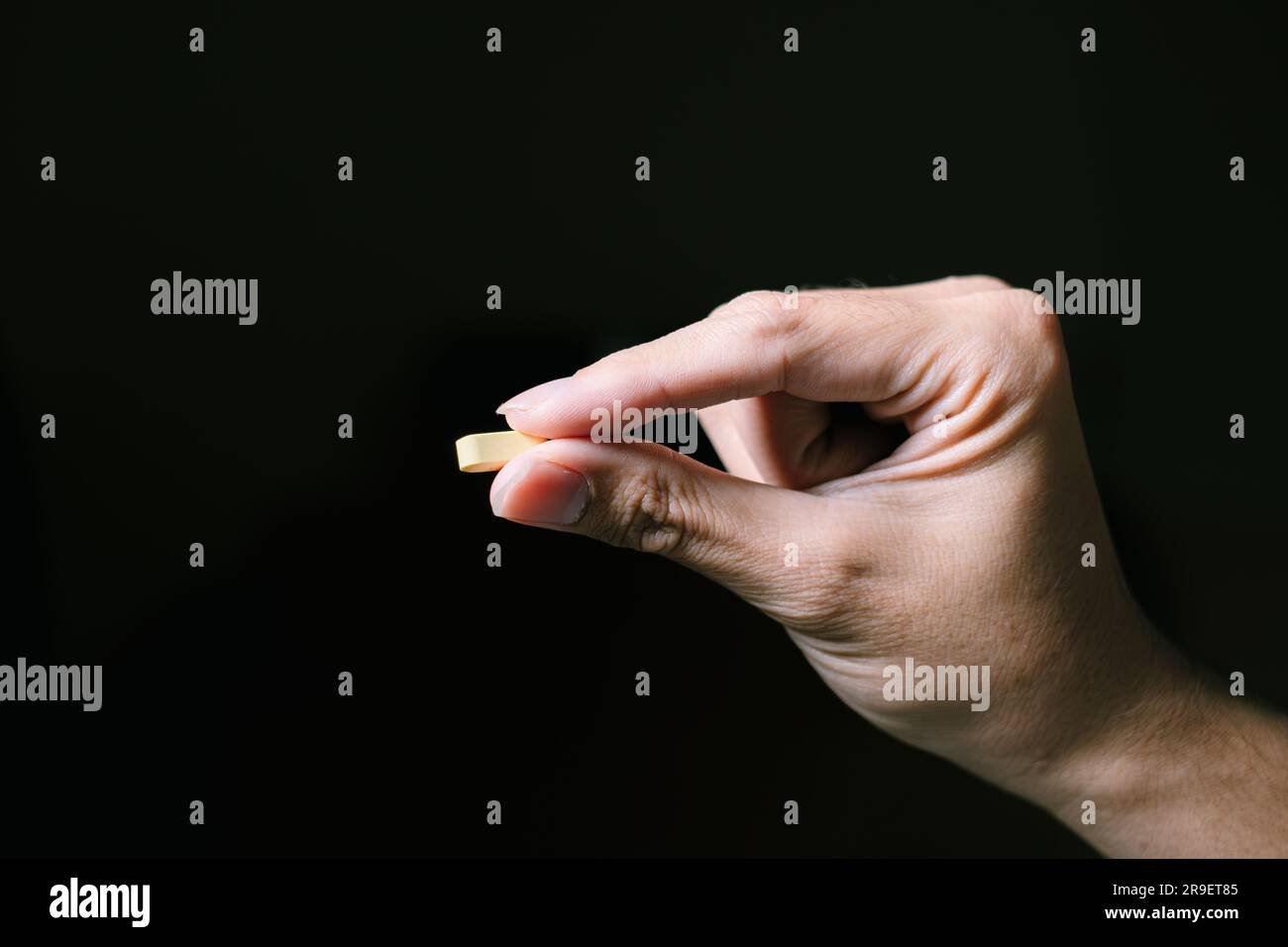 A yellow pill is held by pointing and thumb fingers. Isolated black ...