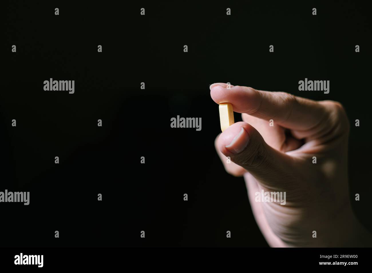 A yellow pill is held by pointing and thumb fingers. Isolated black ...