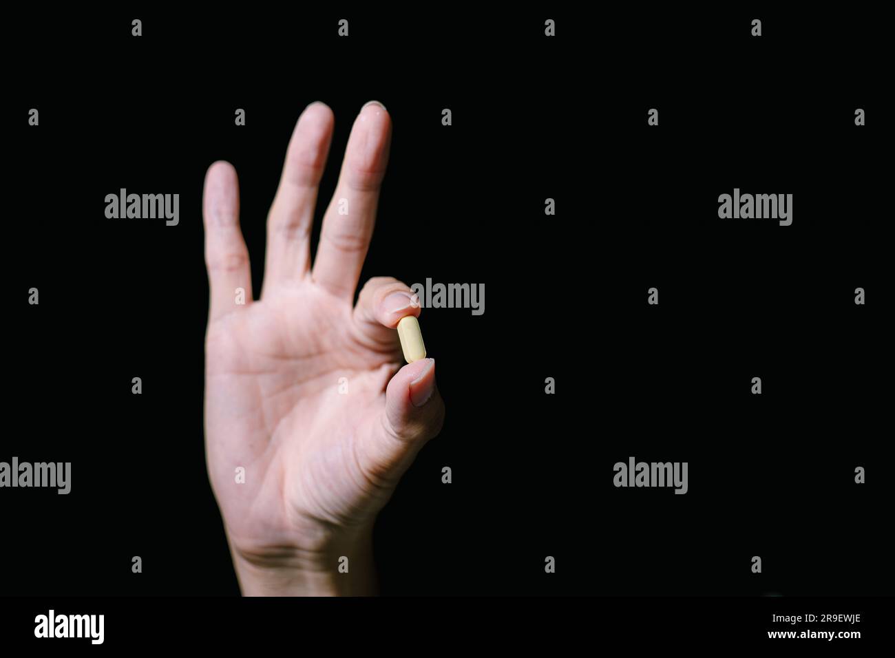A yellow pill is hold by pointing and thumb finger with three other ...