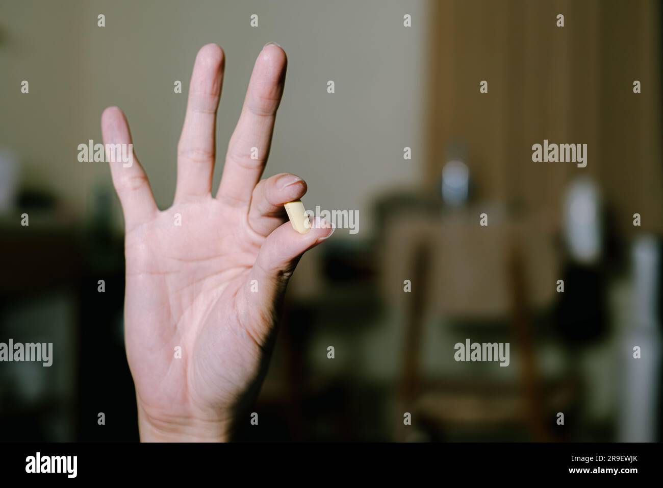 A yellow pill is held by pointing and thumb finger with three other ...