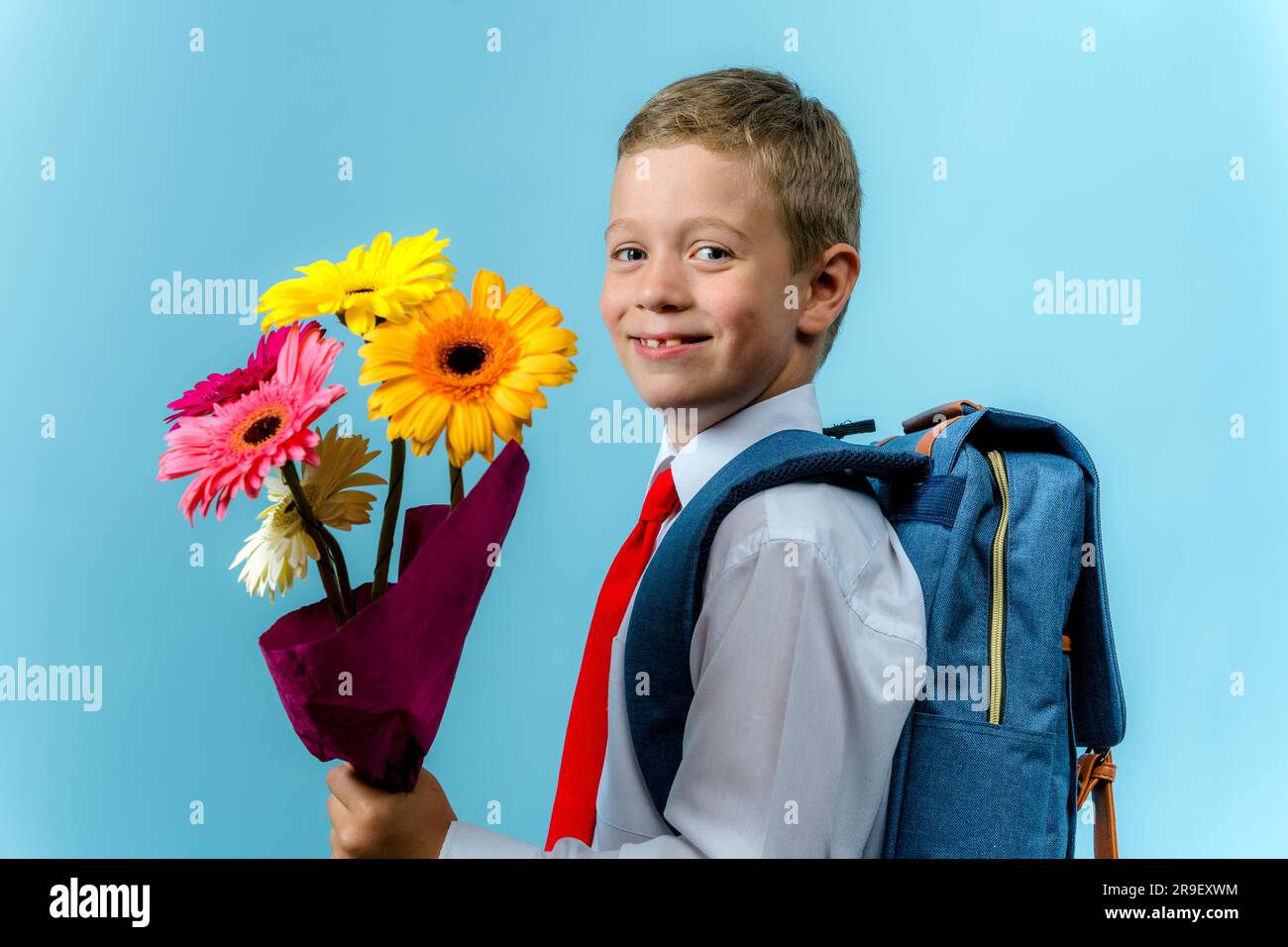 a first grader in a white shirt with a backpack holds a bouquet of ...