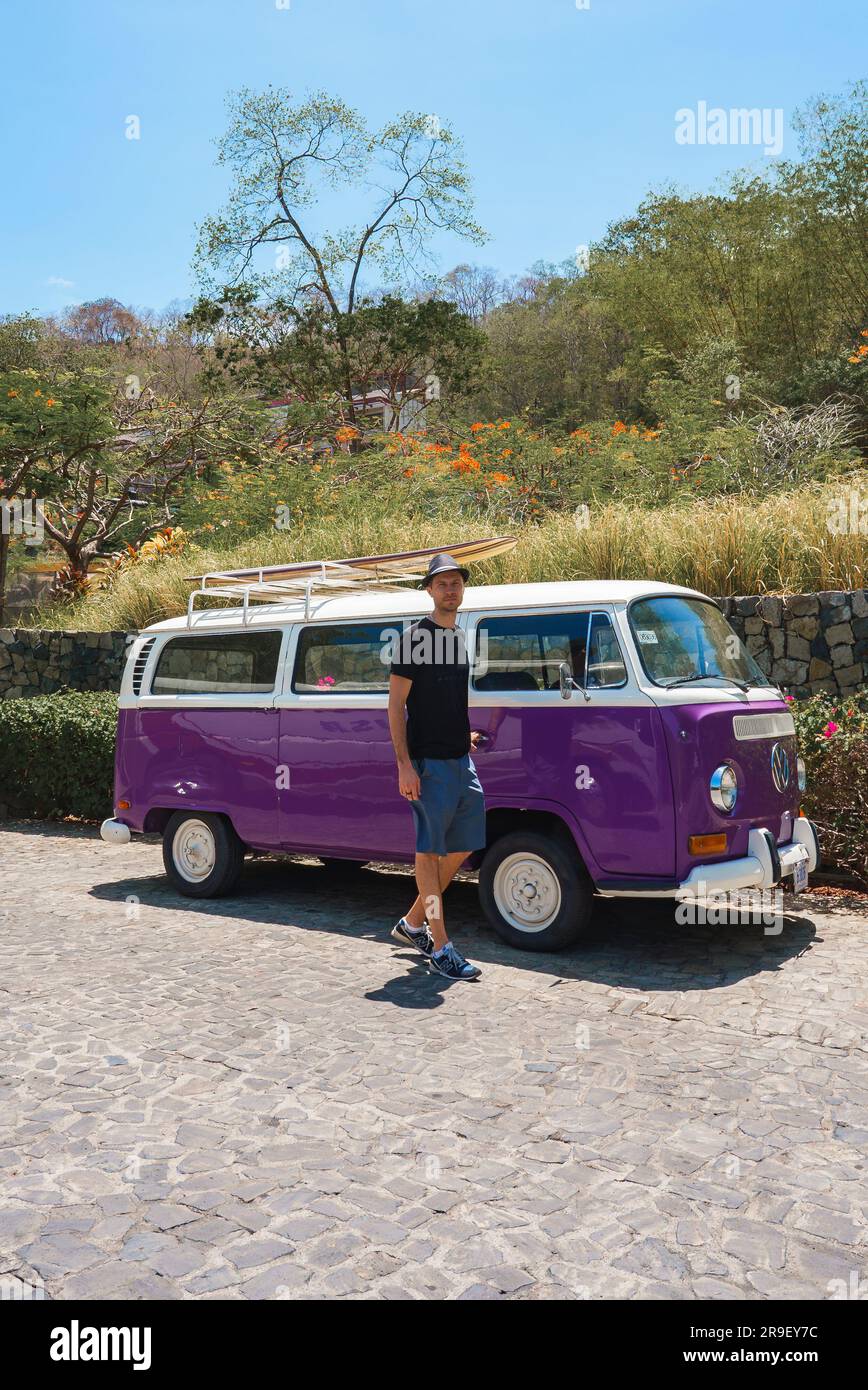 Male traveler standing by classic parked van with surfboard on rack ...