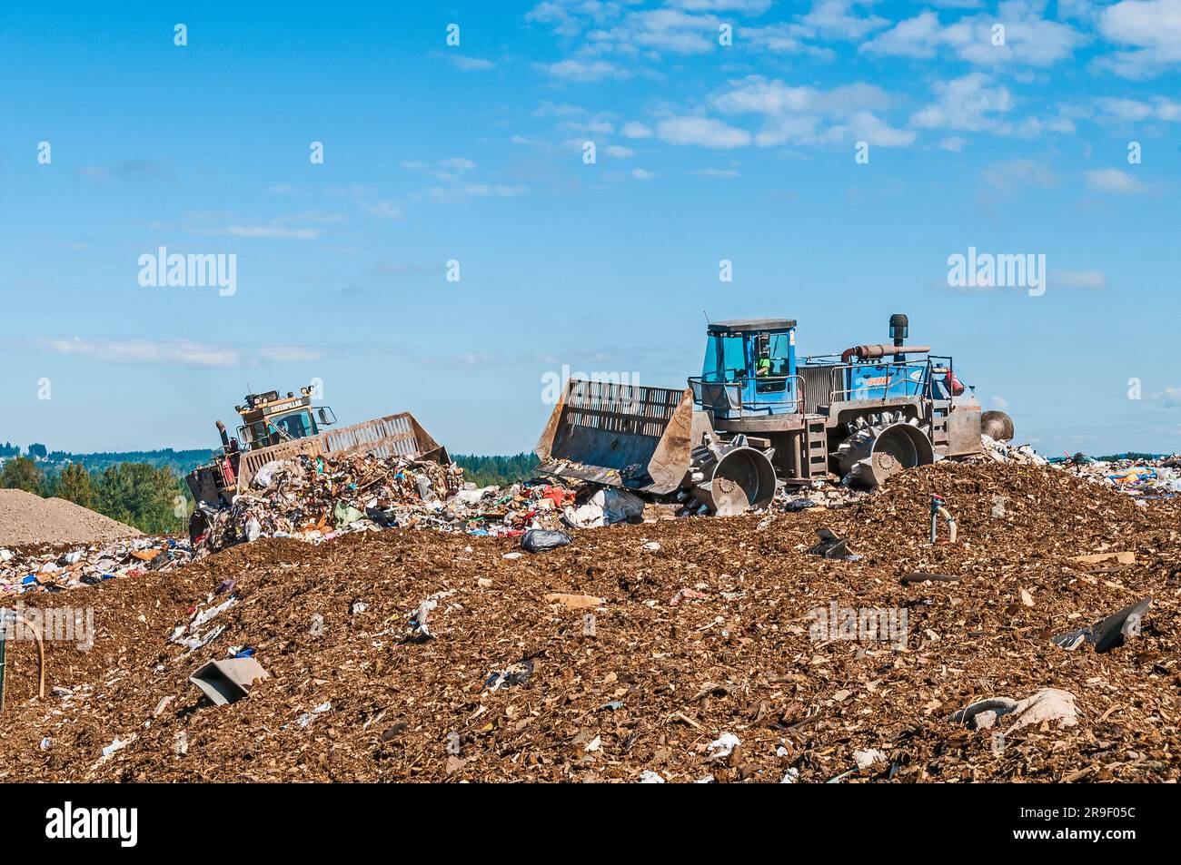 A soil compactor and a bulldozer work the land in an active landfill ...