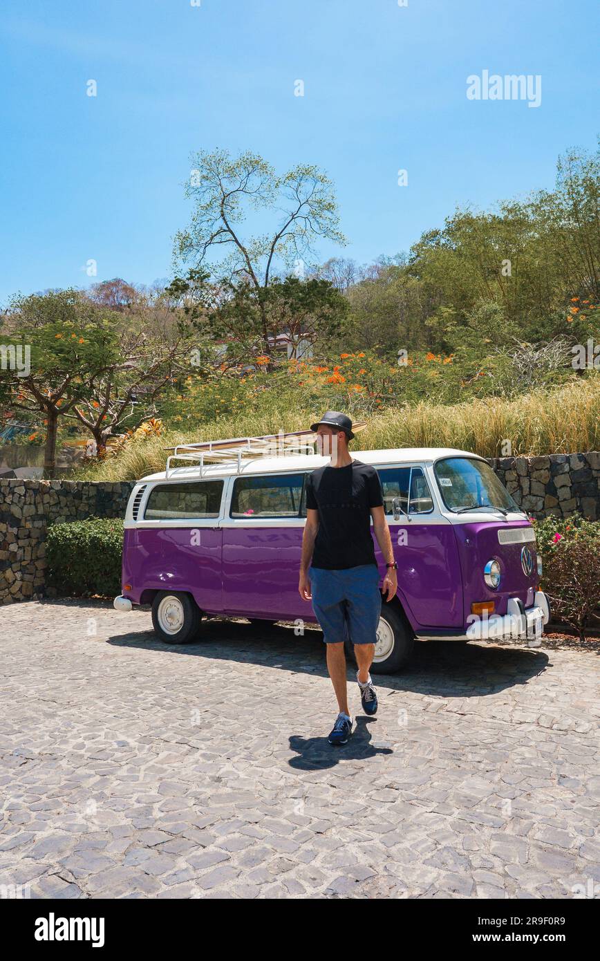 Male traveler standing by classic parked van with surfboard on rack ...