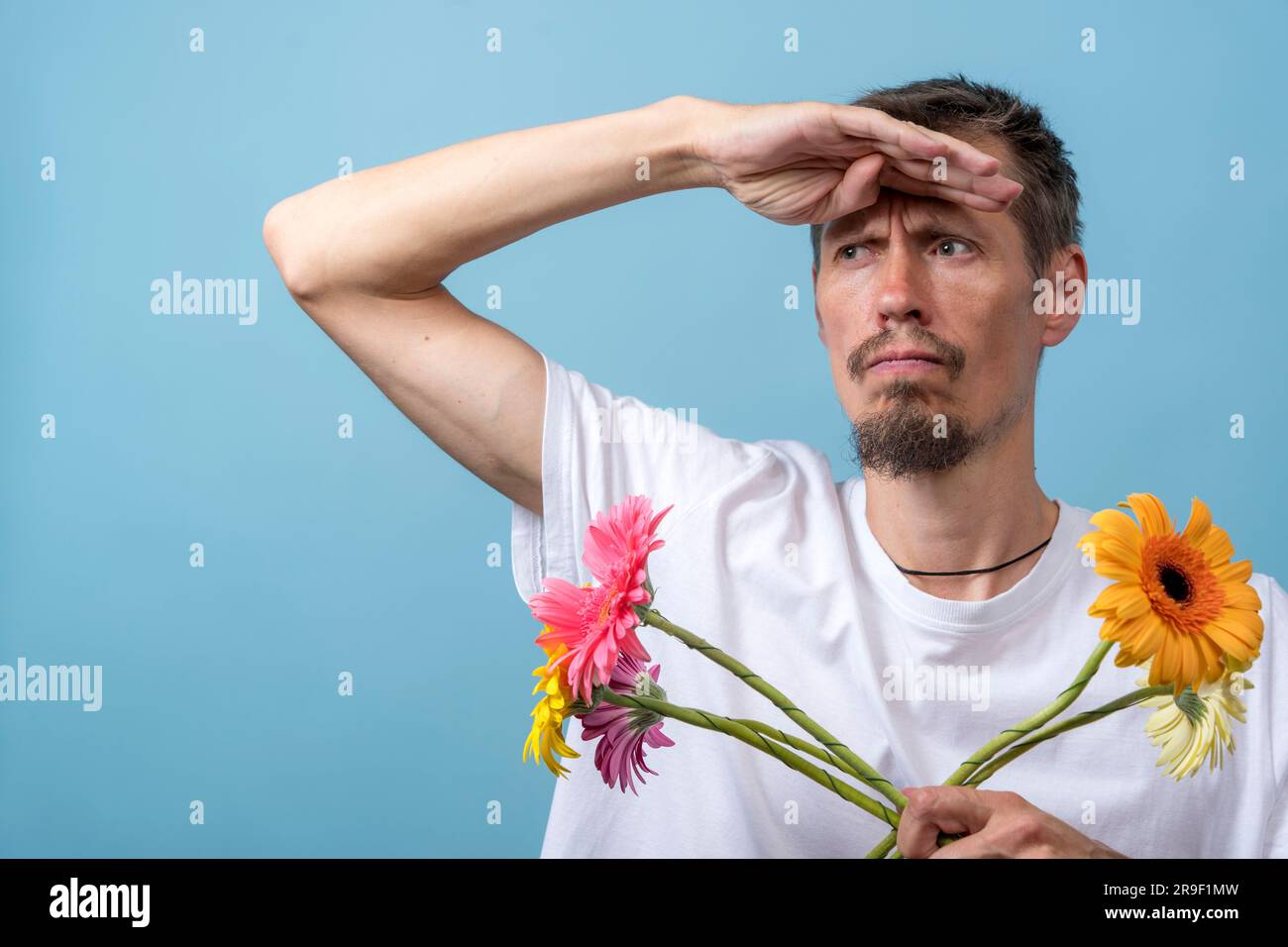 Portrait of a cute Caucasian thoughtful guy with a bouquet of flowers ...