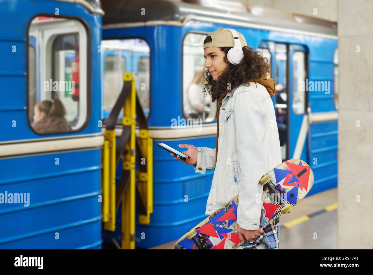 Side view of modern teenager in headphones standing in front of blue ...