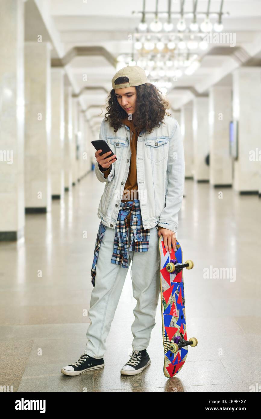 Serious teenage boy with skateboard standing at subway station and ...