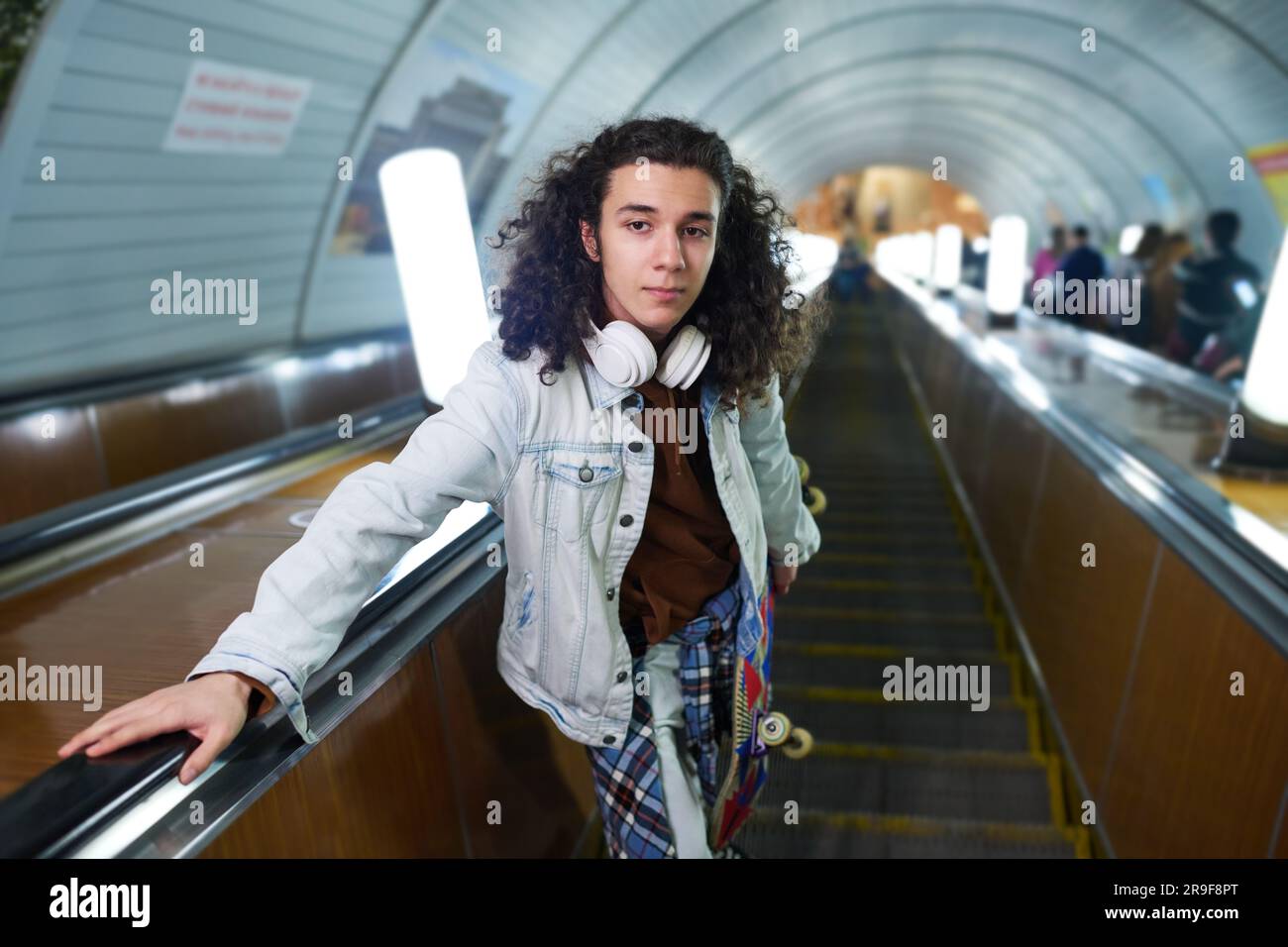 Serious teenage guy with skateboard looking at camera while standing on ...