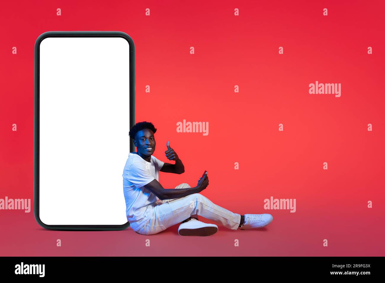 Positive african guy sitting by huge phone with blank screen Stock ...