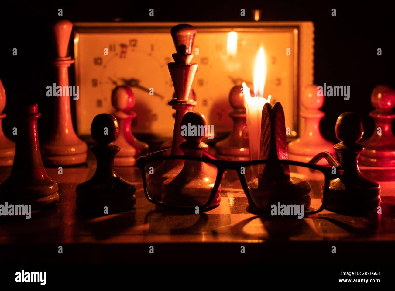 chess pieces stand on a chessboard and clock and next to a burning ...