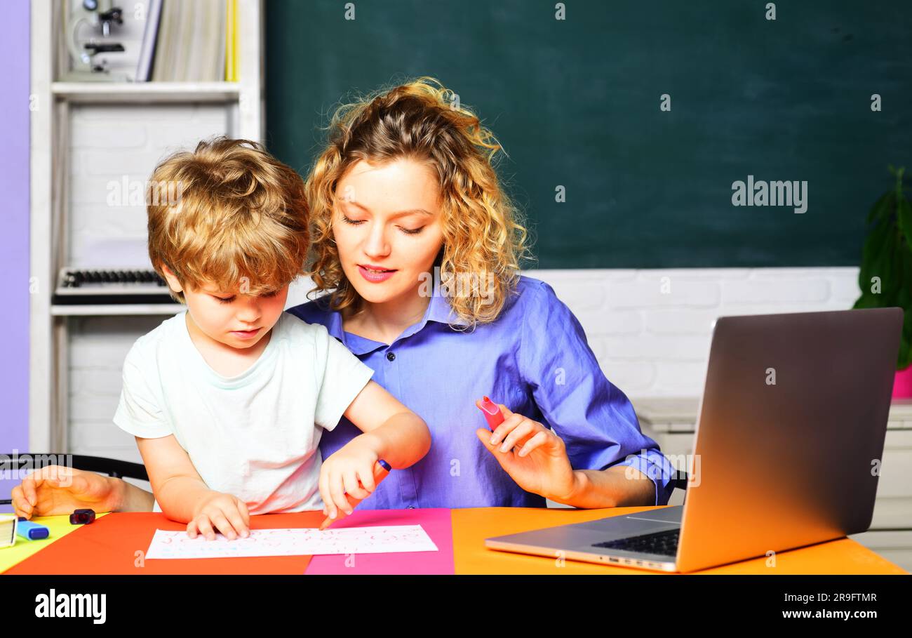 Female elementary school teacher helping little boy with writing lesson ...