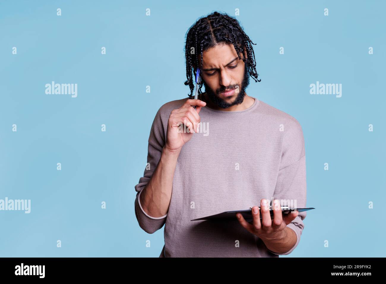 Pensive arab man thinking while holding clipboard and planning ...