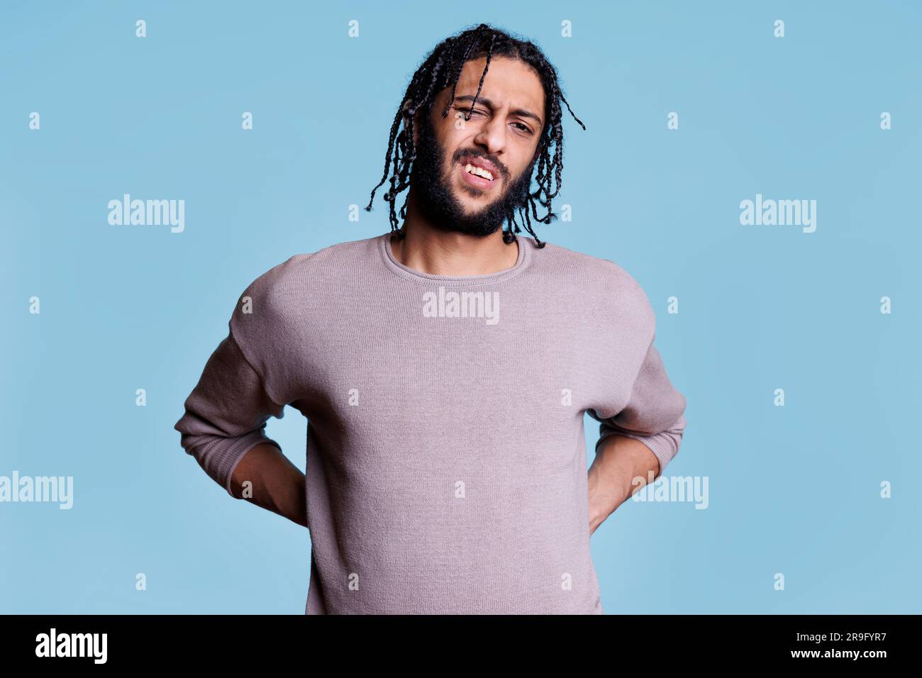 Arab man suffering lower backache and looking at camera with grimace on ...