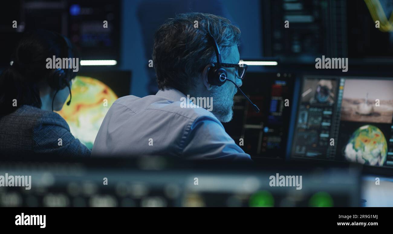 Diverse flight control workers sit in front of computers, monitor space ...