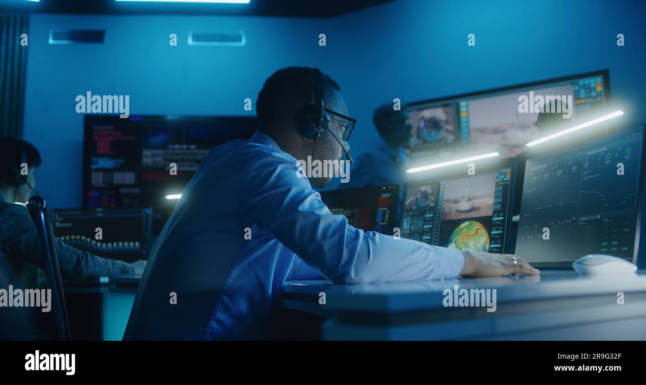 African American flight control employee in headset monitors space ...