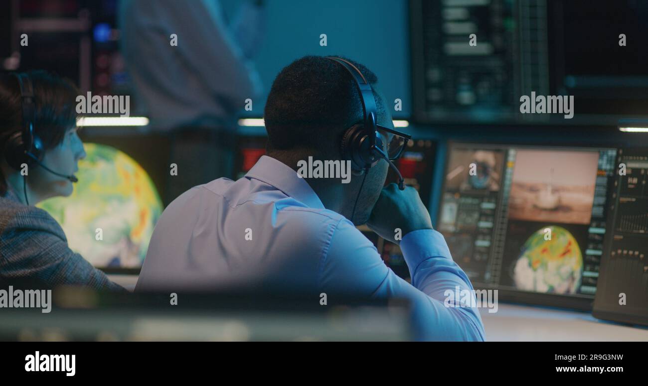 Diverse flight control employees in headsets monitor space mission on ...