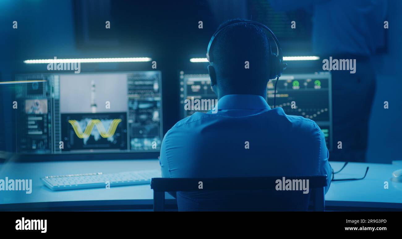 African American flight control employee sits in front of computers ...