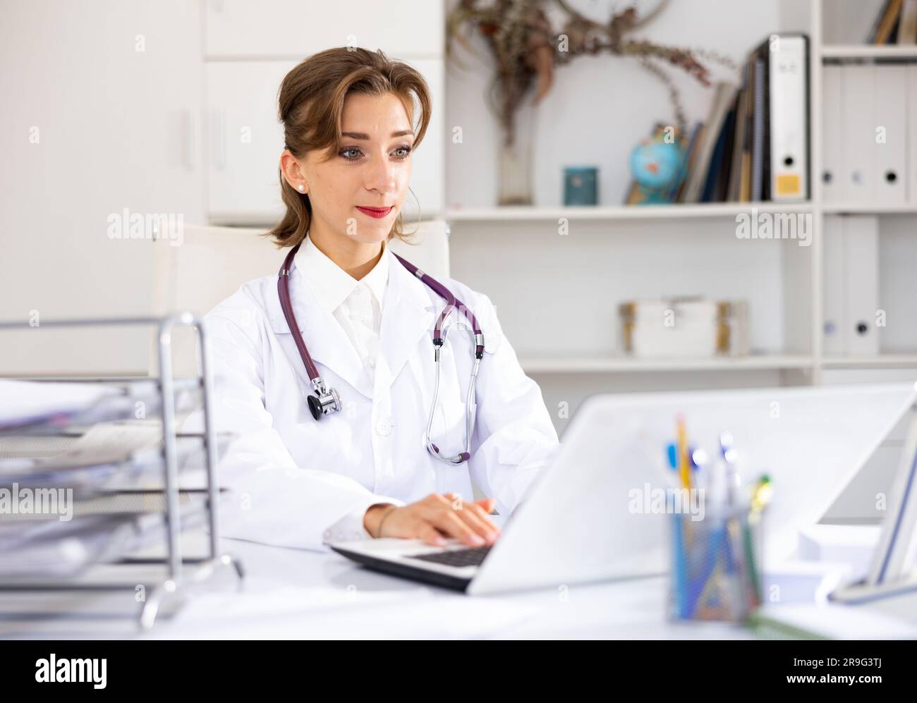 Portrait of female doctor who is working with laptop and documents ...