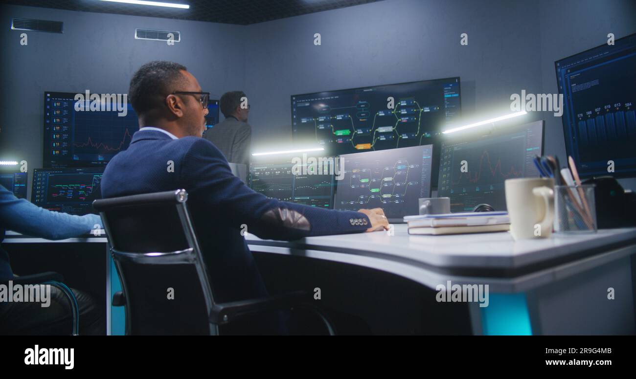 Multiethnic IT technical specialists sit in front of computers with data server in monitoring ...
