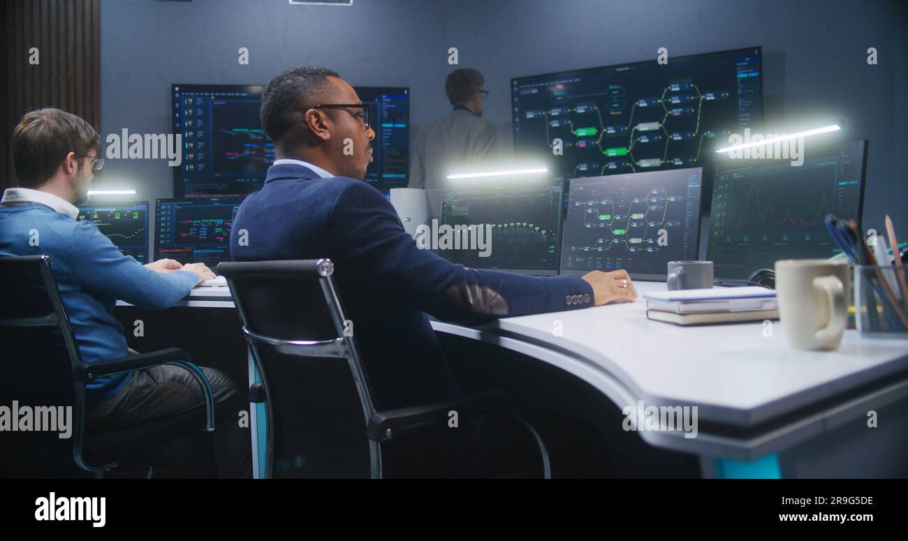 Multiethnic IT technical specialists sit in front of computers with data server in monitoring ...