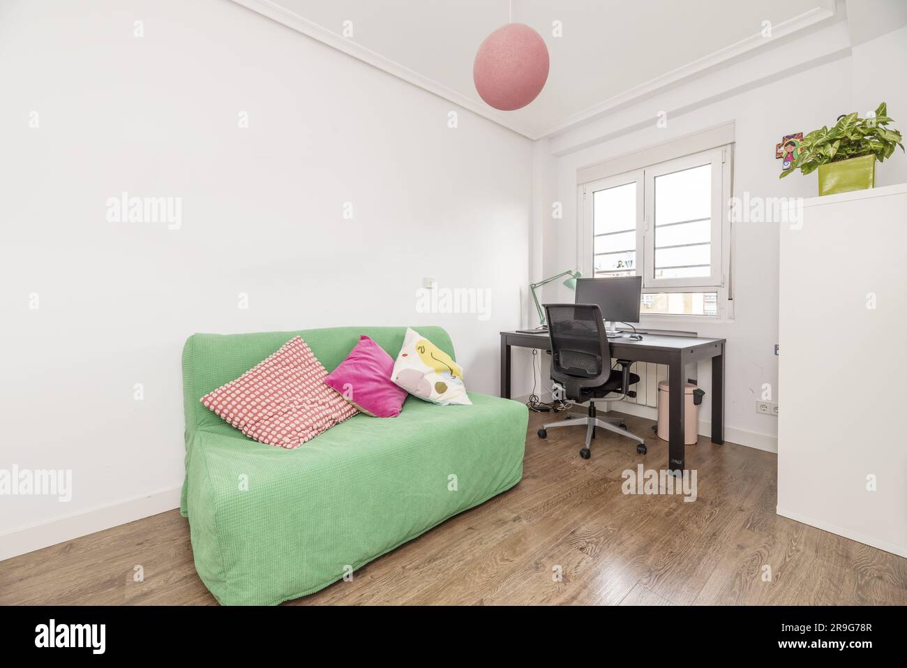 room with green sofa bed, study table with pc and black swivel chair ...