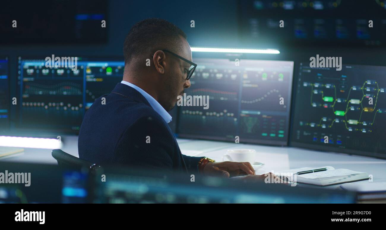 African American software engineer sits in front of computer and big ...