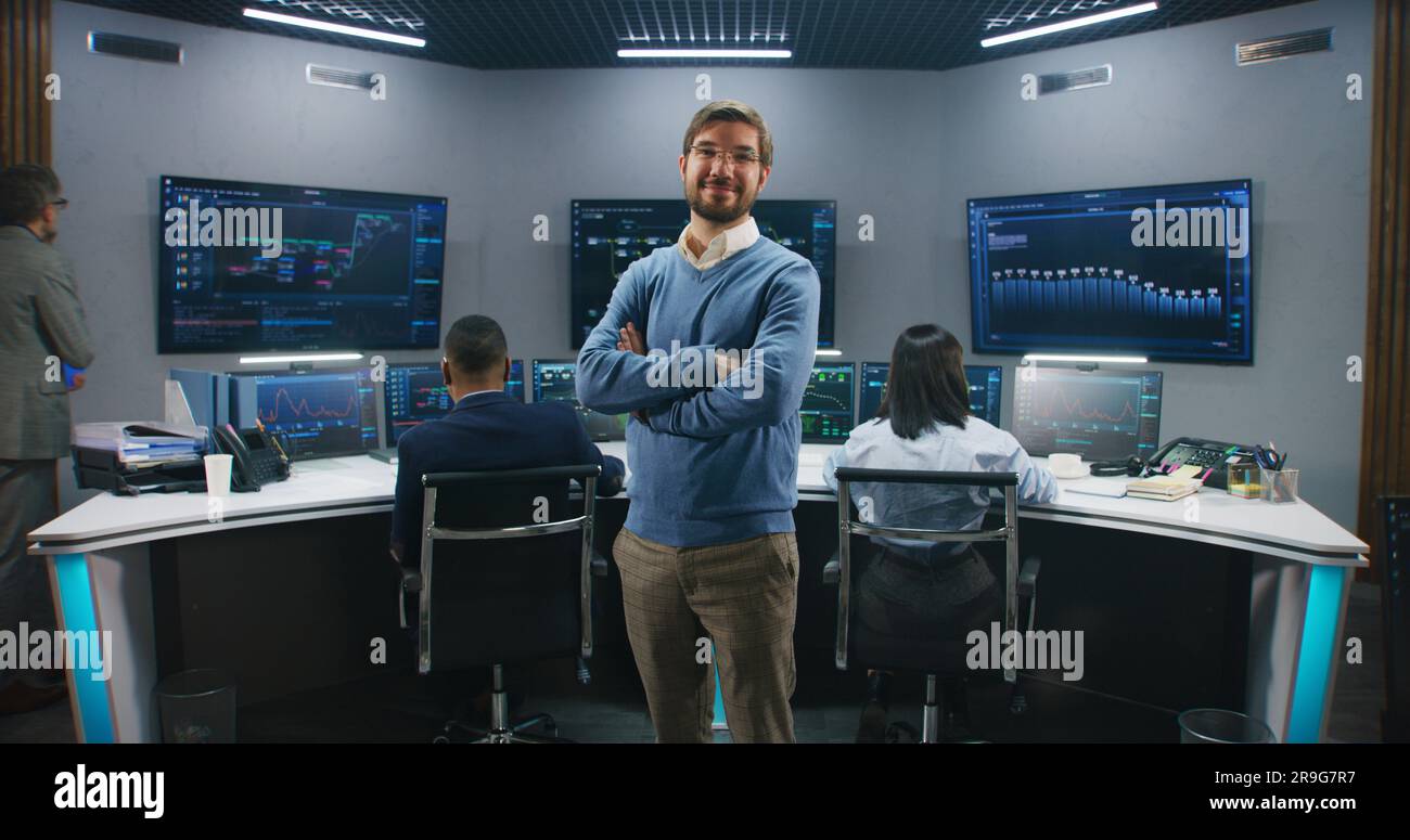 Adult IT scientist smiles, stands in monitoring room and looks at ...