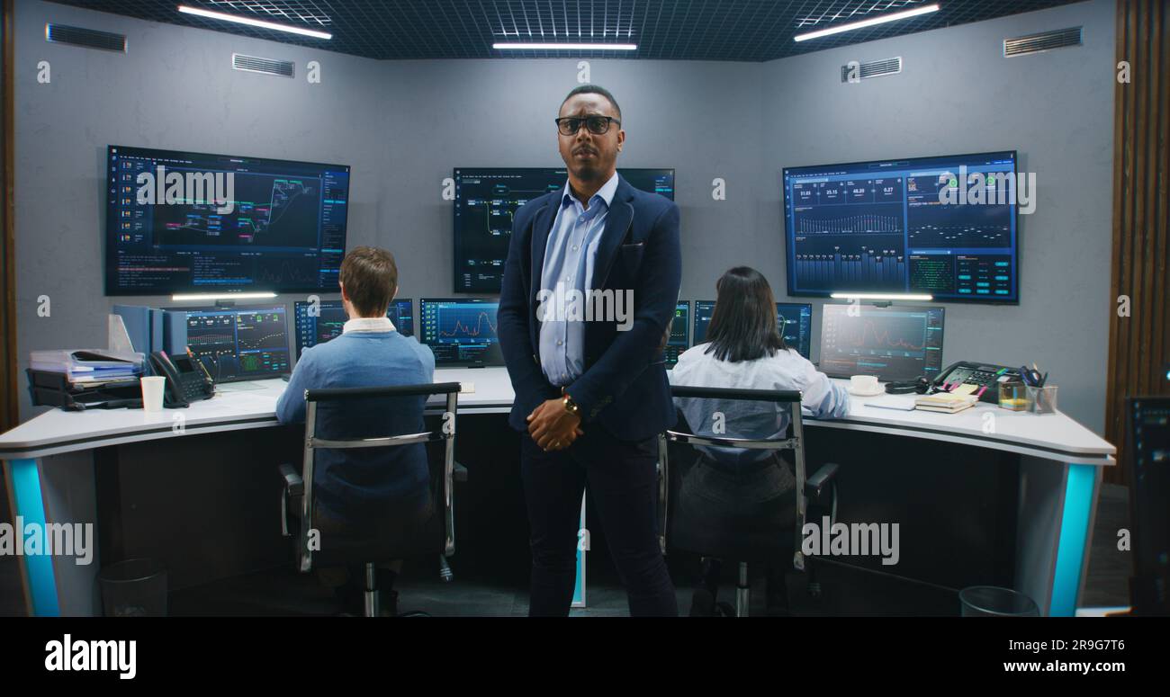 African American IT scientist stands in monitoring room and looks at ...