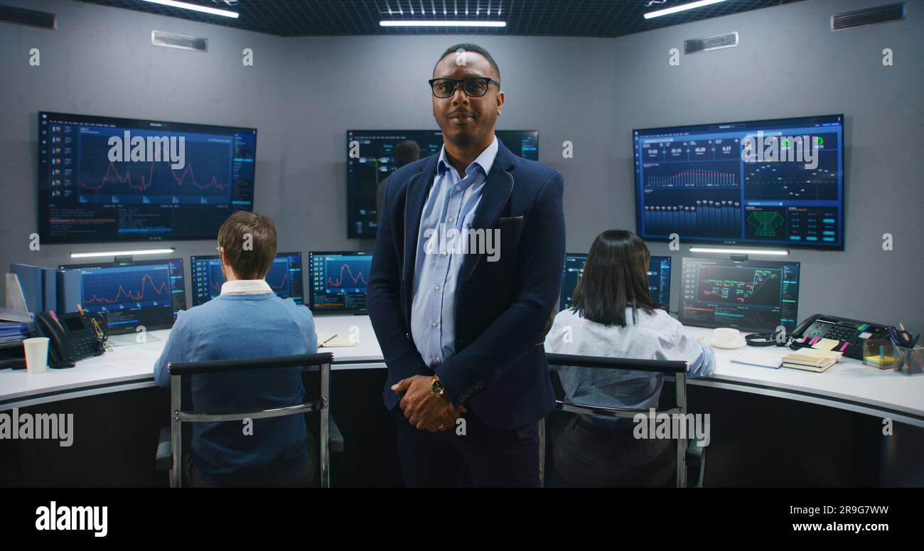 African American IT scientist stands in monitoring room and looks at ...