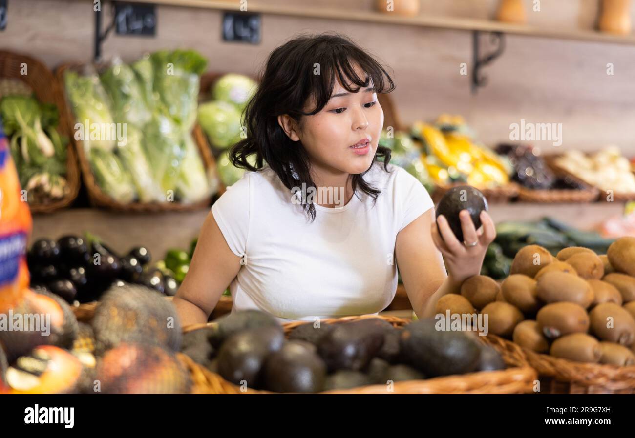 Pleased young woman purchaser choosing avocados in grocery store Stock ...
