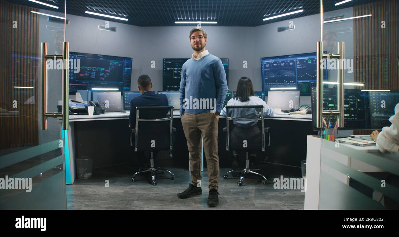 Adult IT scientist smiles, stands in monitoring room and looks at ...