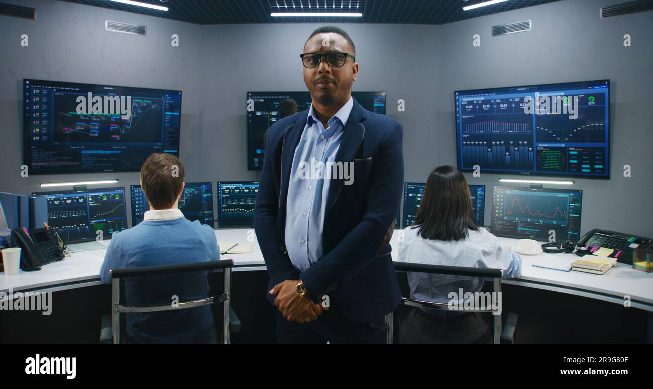 African American IT scientist stands in monitoring room and looks at ...