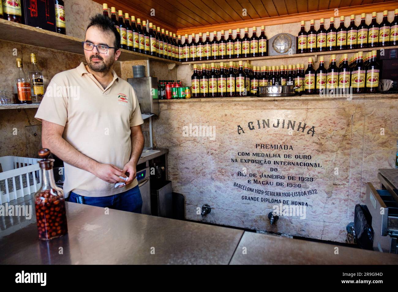 Ginjinha sour cherry liqueur bottles on shelf, worker inside A Ginginha ...