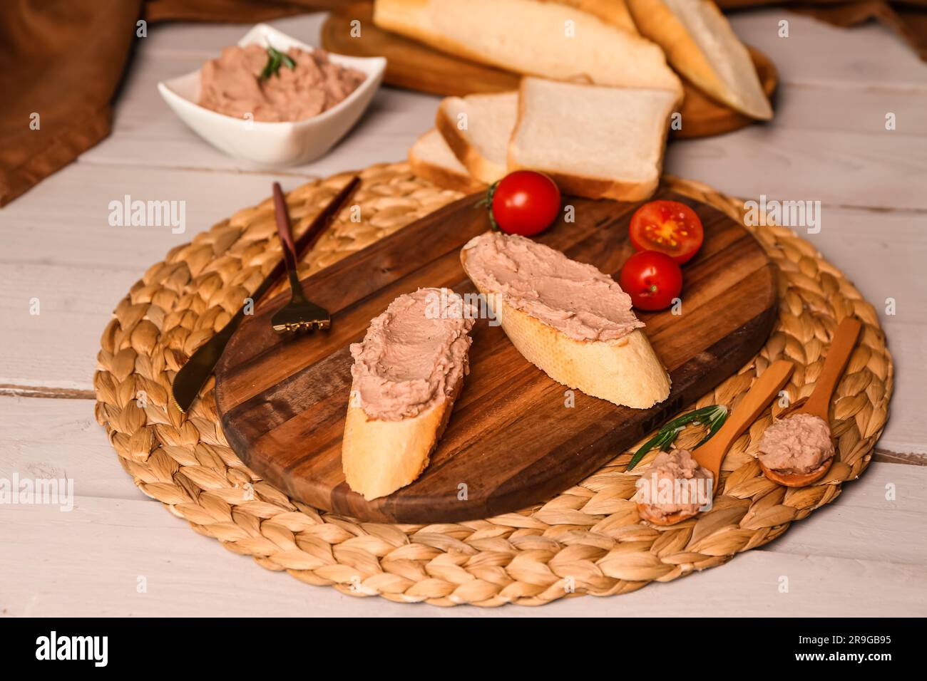 Board of toasts with tasty pate and tomatoes on light wooden table ...