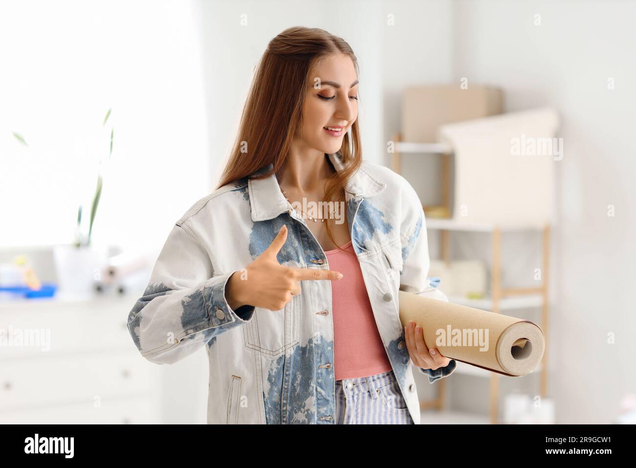 Young woman pointing at wallpaper roll in room Stock Photo - Alamy