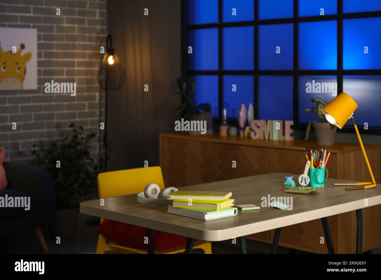 Table with school stationery and lamp in room at night Stock Photo - Alamy