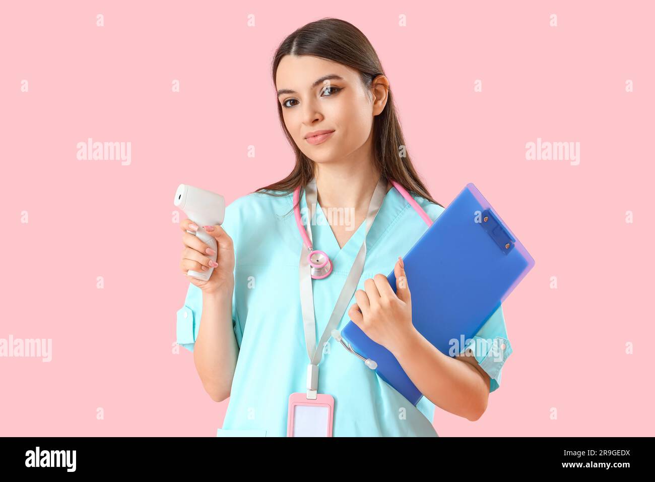 Female medical intern with infrared thermometer and clipboard on pink ...