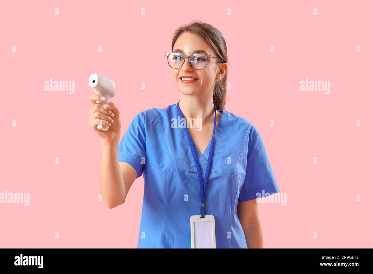Female medical intern with infrared thermometer on pink background ...