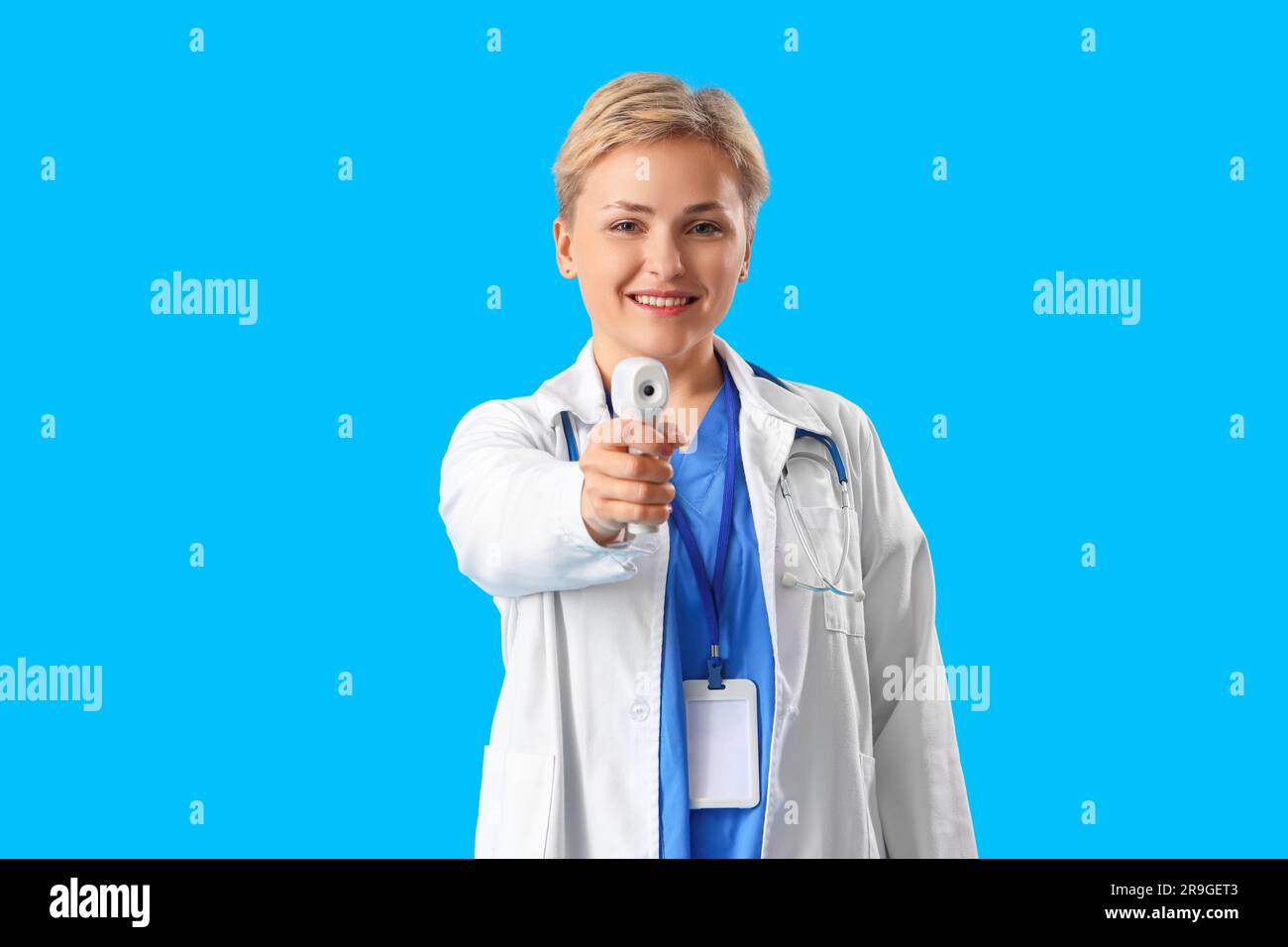 Female medical intern with infrared thermometer on blue background ...