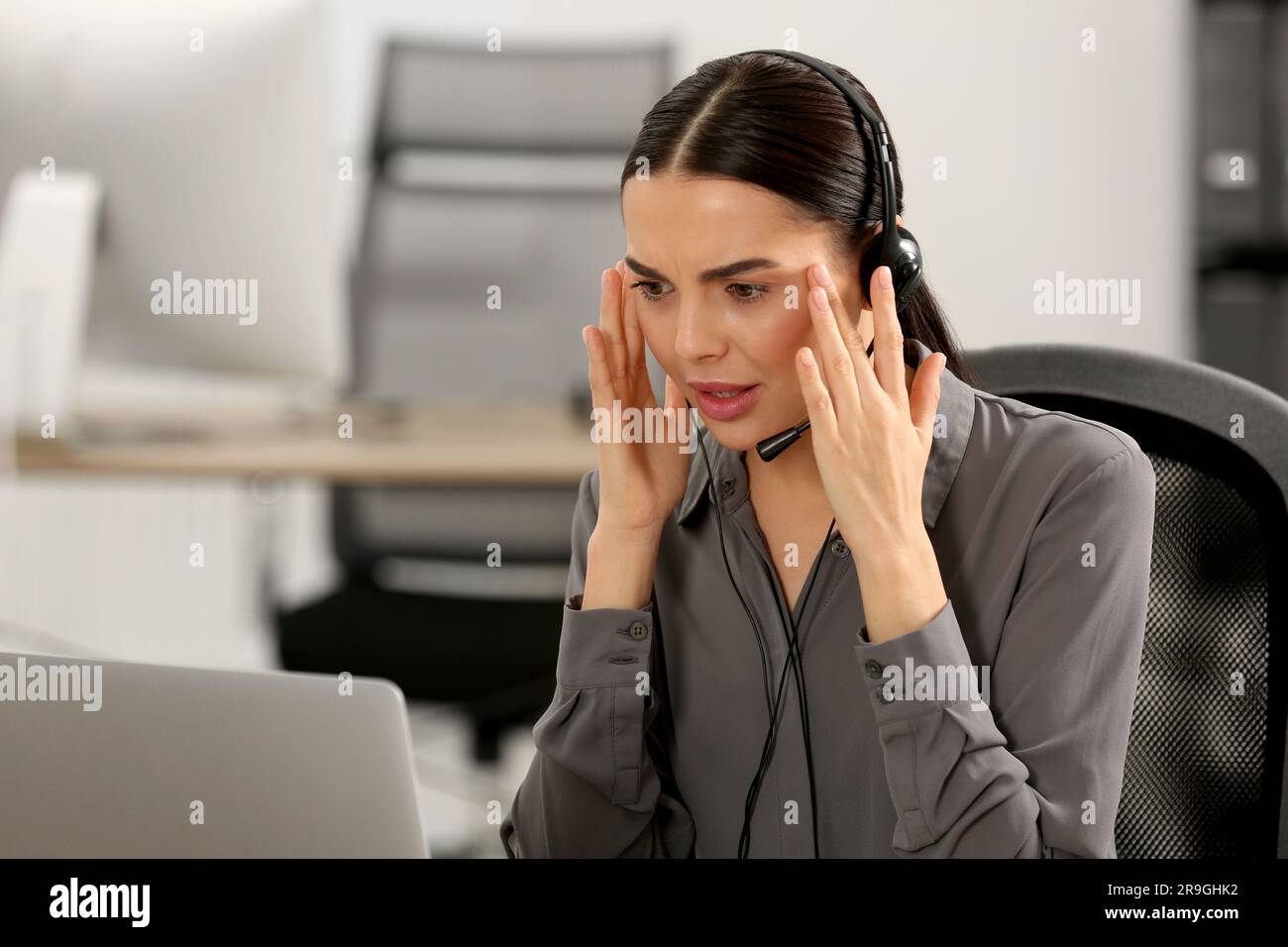 Stressed hotline operator with headset working on laptop in office ...