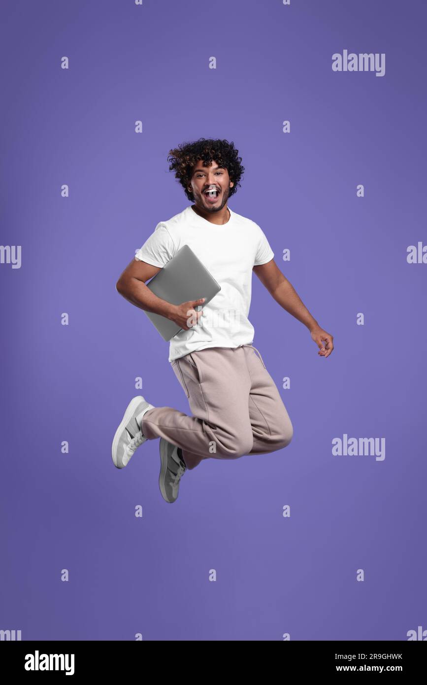 Happy man with laptop jumping on purple background Stock Photo - Alamy