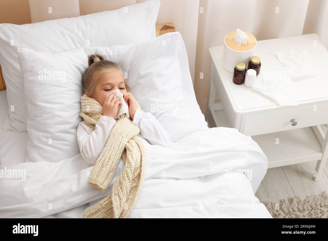 Sick girl with scarf and tissue lying in bed while blowing nose indoors ...